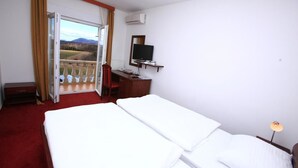 Quarto de hotel com duas camas, uma mesa de trabalho com uma TV, uma janela com vista para o campo e um aparelho de ar condicionado.