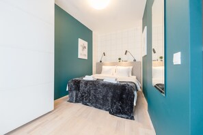 Quarto moderno com cama, abajures, uma pequena planta e um quadro na parede.