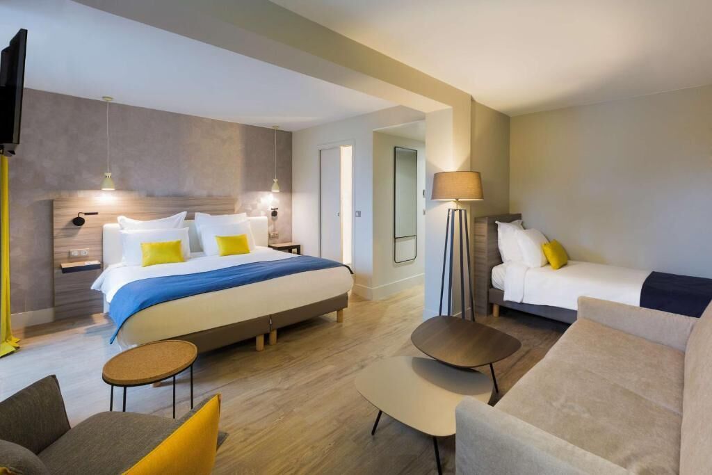 Quarto de hotel com cama grande, mesas de cabeceira, escrivaninha, sofá e abajur.