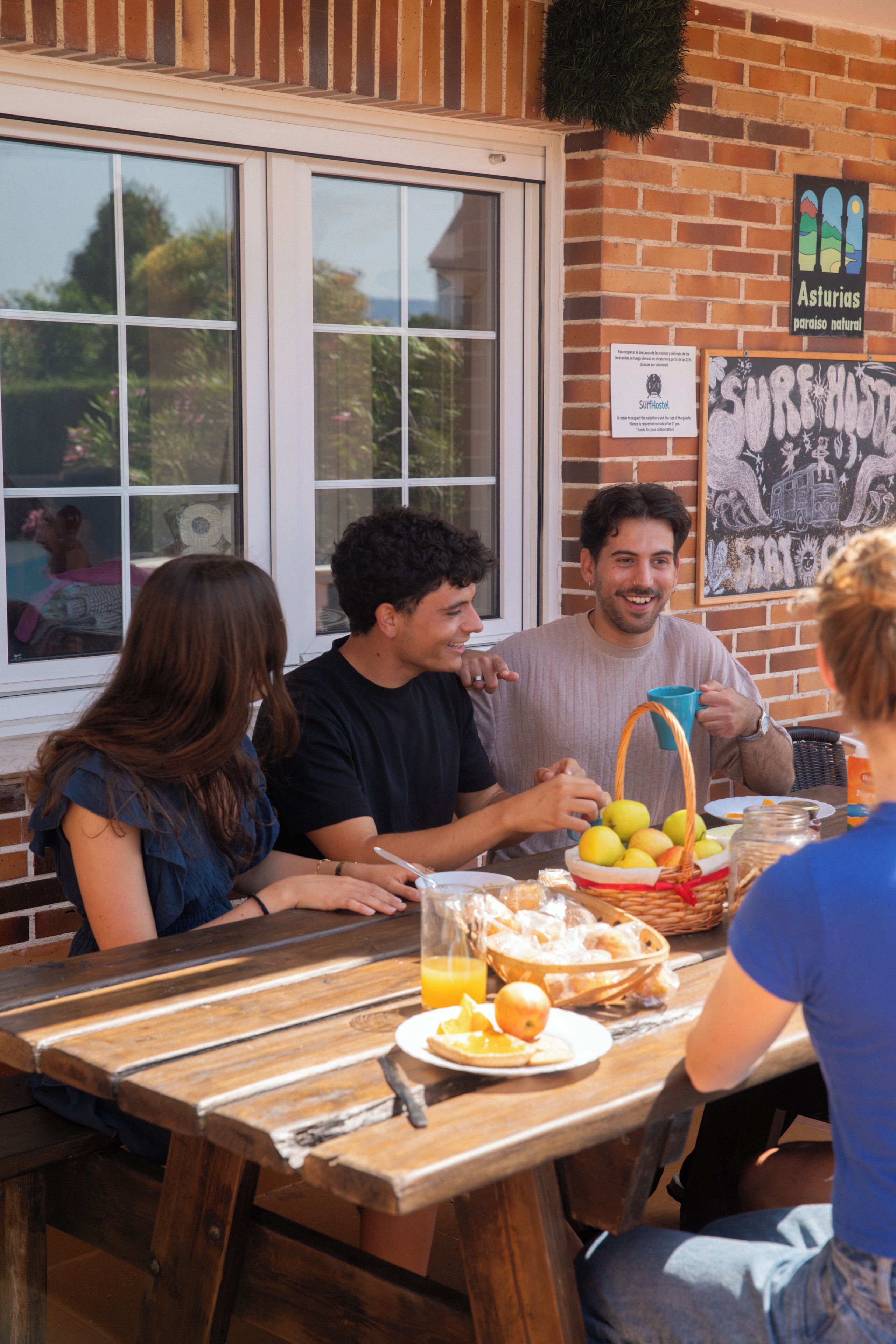 Um grupo de pessoas sentadas à mesa de madeira, com uma cesta de frutas e um copo de suco de laranja.