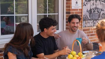 Um grupo de pessoas sentadas à mesa de madeira, com uma cesta de frutas e um copo de suco de laranja.