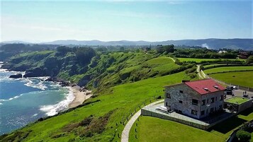 Um imóvel costeiro com um edifício grande, uma praia e colinas suaves ao fundo.