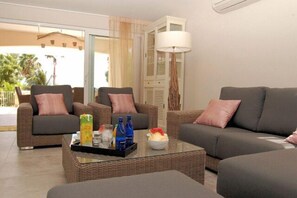 Uma sala de estar com dois sofás, uma mesa de centro com bebidas e uma janela grande com cortinas.