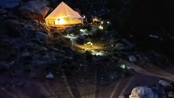 Alojamento em tenda com um quarto único, rodeado por terreno rochoso e vegetação escassa.