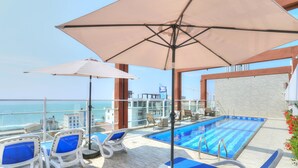 Área da piscina com espreguiçadeiras e guarda-sóis, com vista para o mar.
