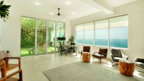 Uma sala de estar espaçosa, com grandes janelas, uma mesa de centro de madeira e vista para o mar.