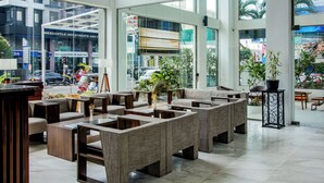 Um espaço de estar interno moderno, com pé-direito alto e grandes janelas, apresentando uma combinação de sofás e mesas, além de plantas em vasos.