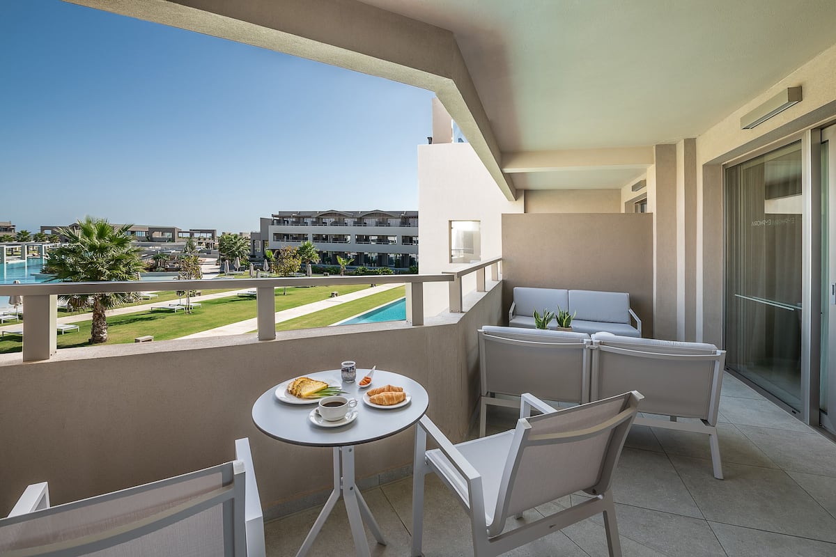 Varanda com vista para a piscina, mobiliário branco e mesa de jantar com comida e bebidas.