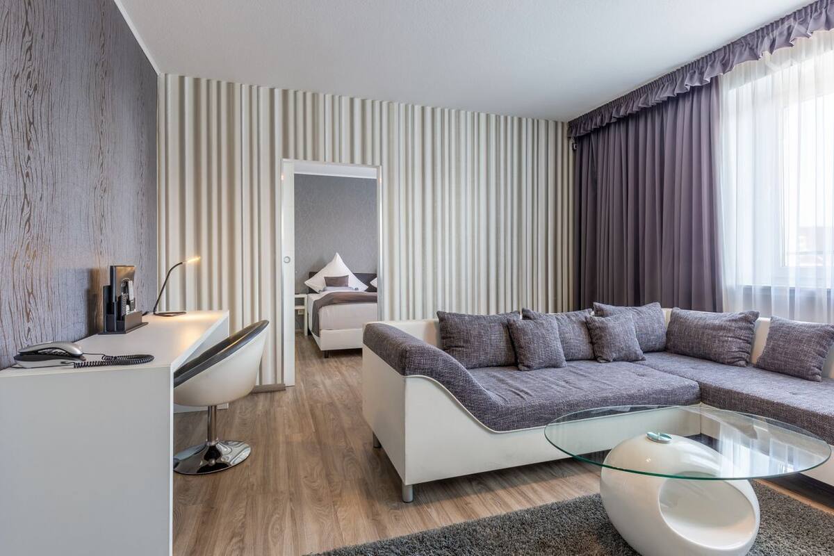 Uma sala de estar moderna com um sofá, uma mesa de centro de vidro e uma escrivaninha com abajur.