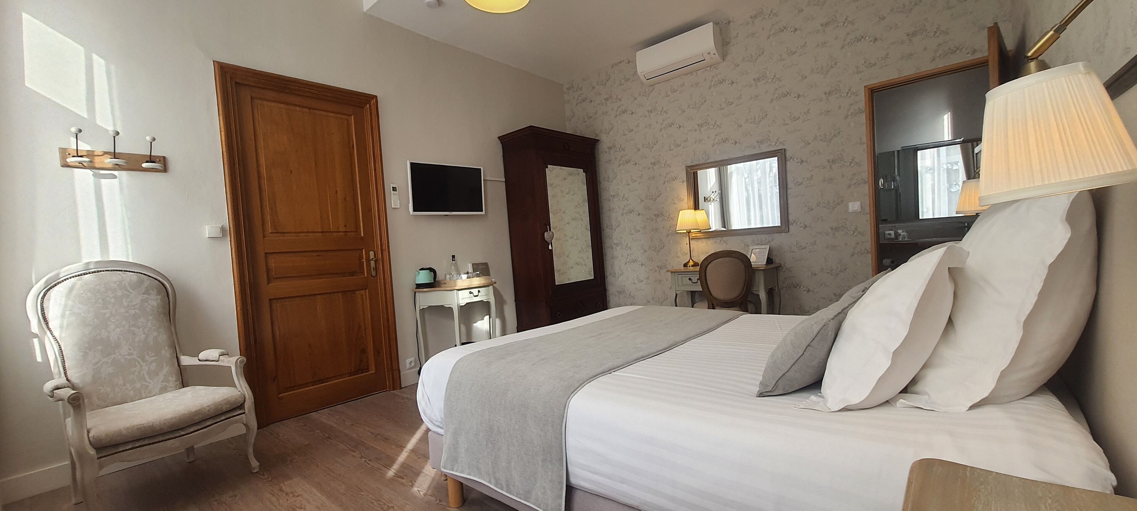 Quarto com cama, cadeira, escrivaninha, televisão e espelho.