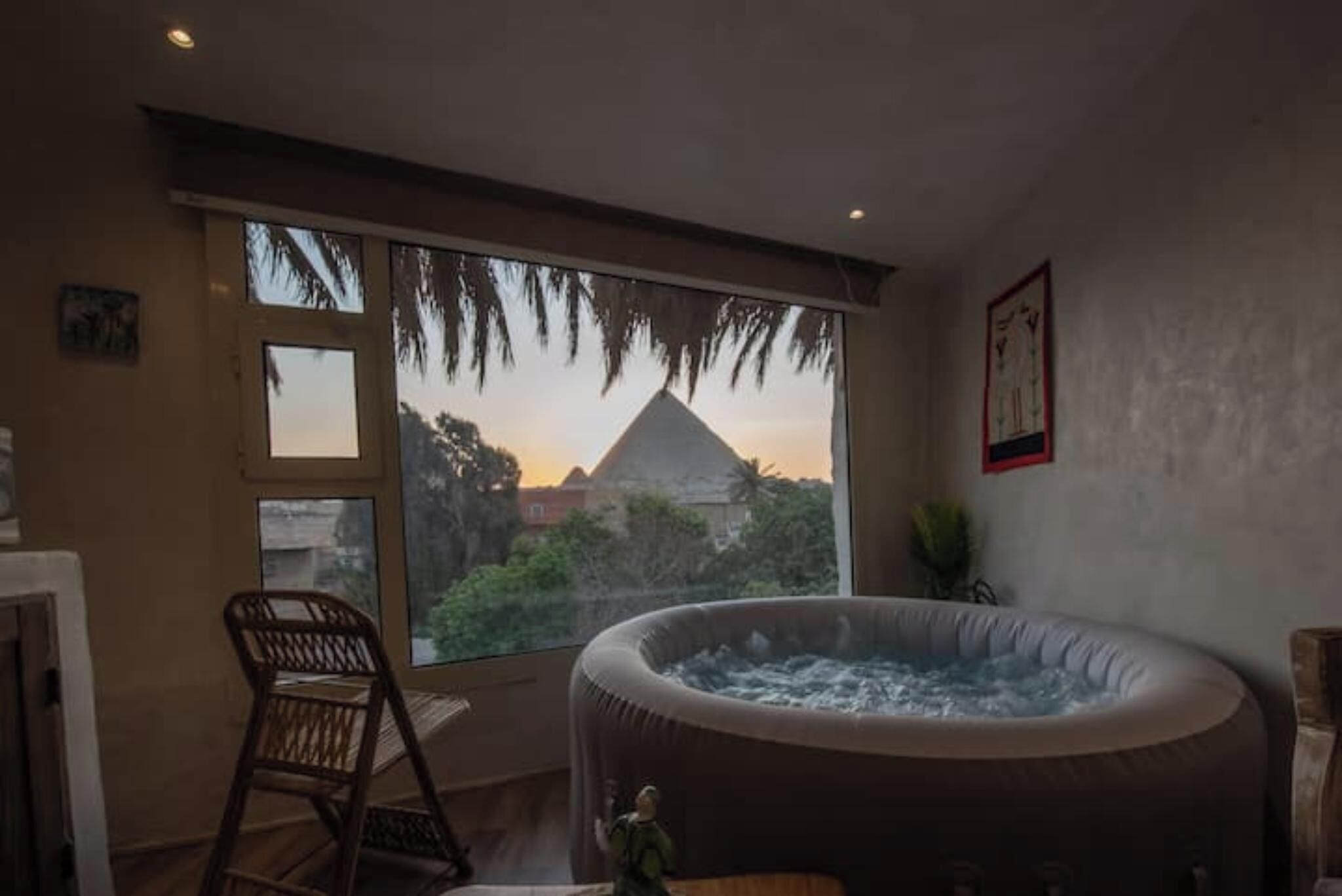 Quarto com hidromassagem, uma poltrona e uma janela grande com vista para uma pirâmide.