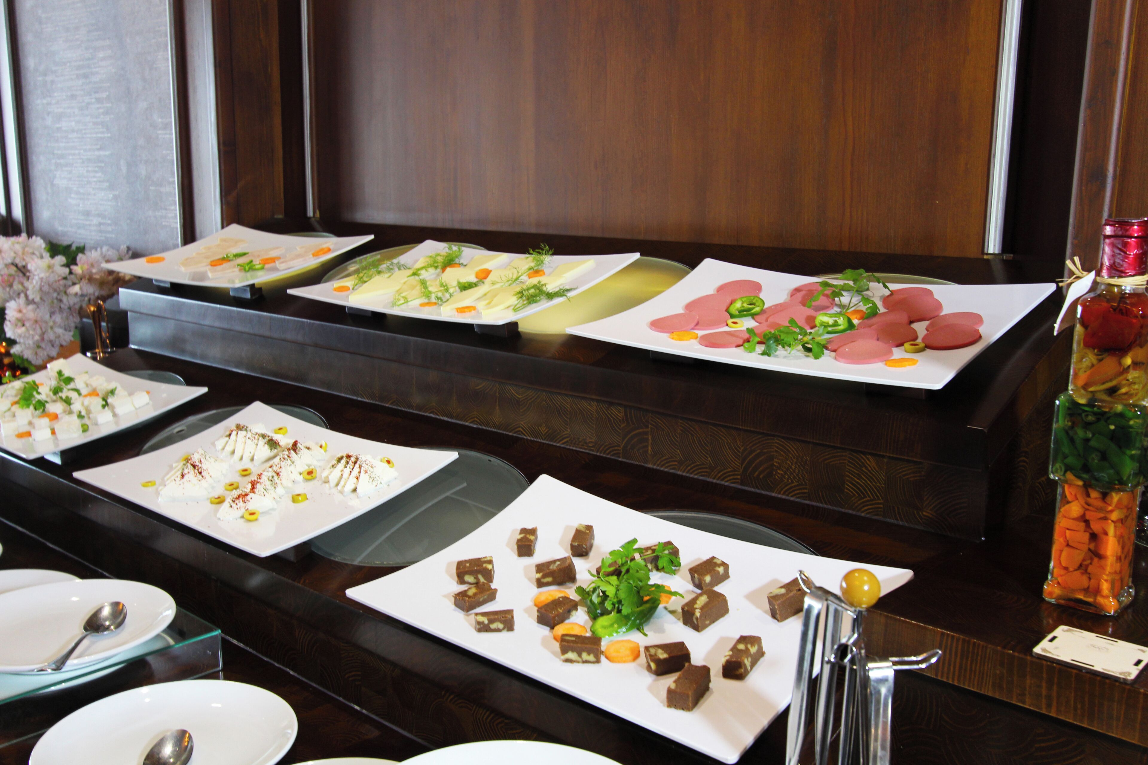 Buffet com diversos pratos, incluindo saladas, carnes e sobremesas, dispostos em pratos brancos.