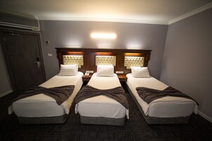 Quarto de hotel com três camas de solteiro, cabeceira de madeira, mesa de cabeceira com telefone e porta com puxador.