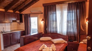 Quarto com cama grande, mesa de cabeceira, cortinas na janela e cozinha equipada com armários e pia.