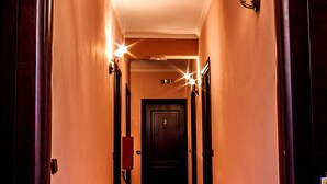 Um corredor com piso de azulejos, uma porta com o número 3 e arandelas com luzes.
