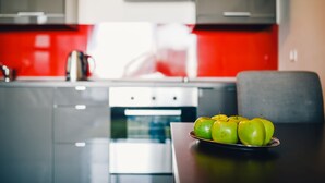 Uma cozinha moderna com revestimento vermelho, eletrodomésticos de aço inoxidável e um prato de maçãs verdes na bancada.