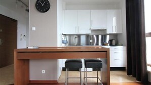 Cozinha moderna com armários brancos, eletrodomésticos de aço inoxidável e uma ilha de madeira com dois banquetas.