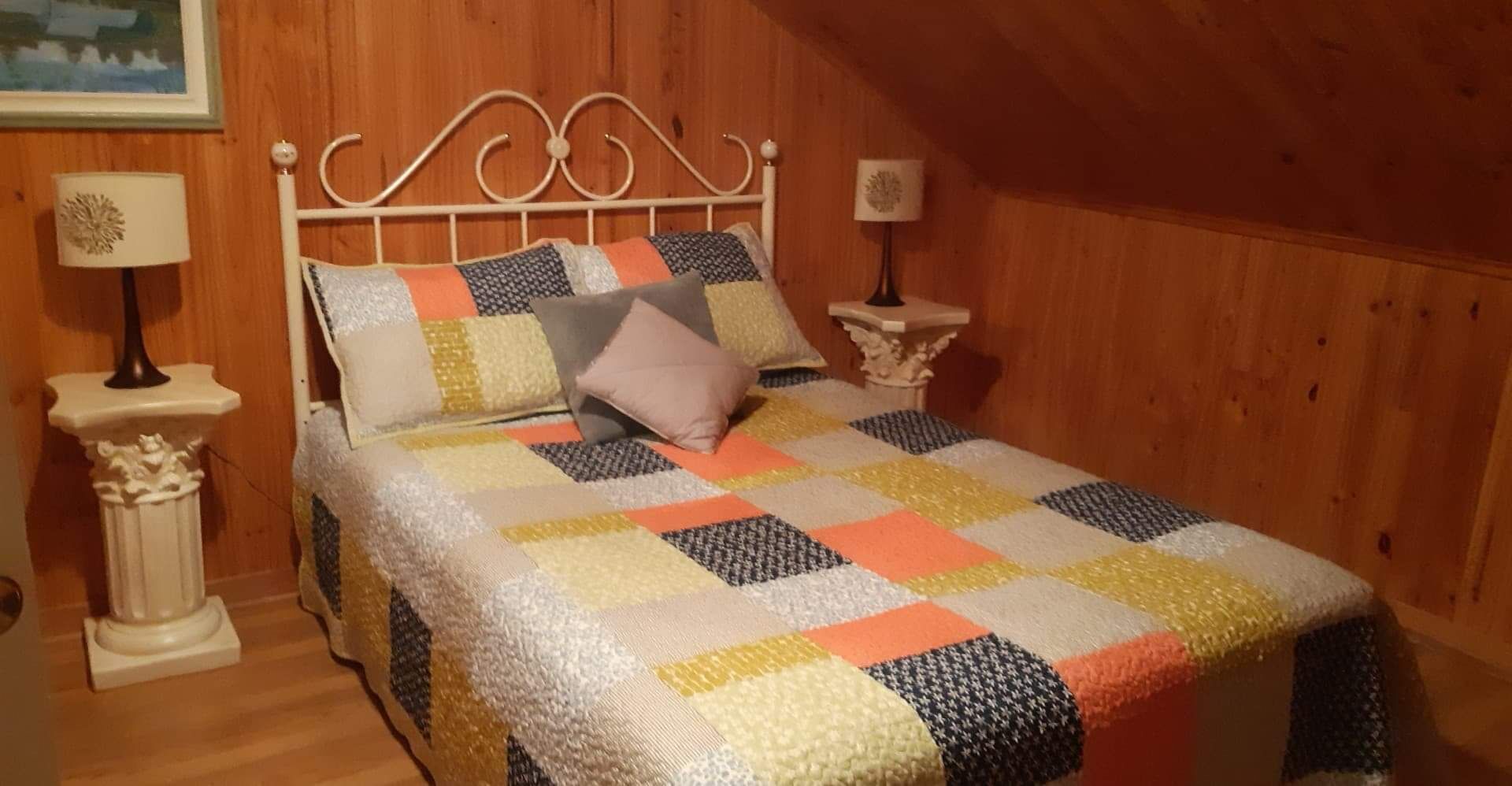 Quarto com cama, duas mesinhas de cabeceira e parede de madeira.