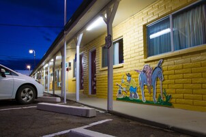 Um motel com fachada amarela, um mural de um cavaleiro e um carro branco estacionado na frente.