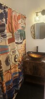 Casa de banho com cortina de chuveiro representando a Rota 66, pia de madeira e luminária fixada na parede.