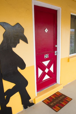 Uma porta vermelha com o número 20, um tapete de boas-vindas e o contorno de uma pessoa na parede.
