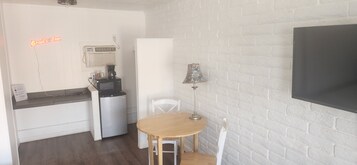 Uma cozinha compacta com cafeteira, geladeira e um letreiro neon com a inscrição 'Brad's Inn'.