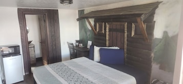 Quarto com cama, escrivaninha, cadeira, micro-ondas e pequeno frigorífico.