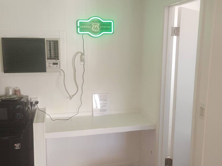 Quarto com micro-ondas, cafeteira, mini-geladeira, ar-condicionado fixado na parede e um letreiro de neon indicando posto de serviço.