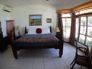 Quarto com uma cama grande, duas luminárias de cabeceira, um guarda-roupa de madeira, um quadro na parede e uma janela com cortinas.