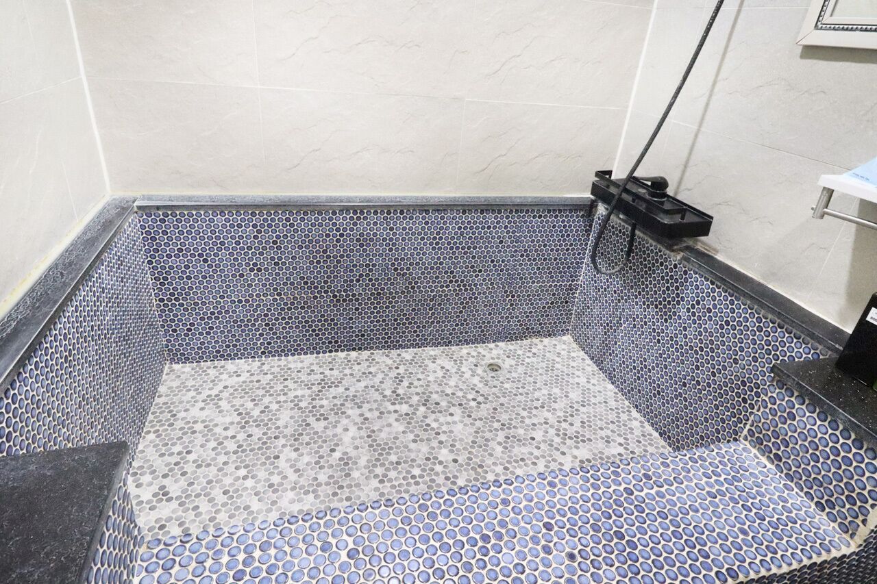 Chuveiro com chão revestido em azulejos azuis e brancos e um chuveiro de cor preta.