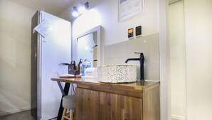 Casa de banho compacta com toucador de madeira, lavatório com cuba estampada, espelho e frigorífico.