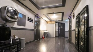 Corredor de hotel com placa de área de cuidado, mini refrigerador, lixeira e extintor de incêndio.