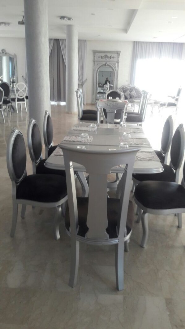 Uma sala de jantar com mesa redonda posta para seis pessoas, rodeada por cadeiras com assentos acolchoados e estrutura metálica.