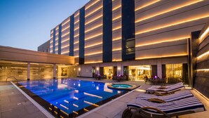 Um hotel moderno com uma grande piscina ao ar livre, espreguiçadeiras e uma entrada bem iluminada.
