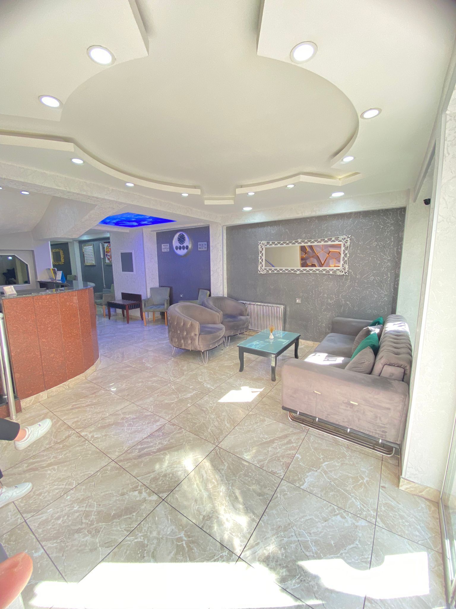 Um hall amplo com balcão de recepção, área de estar e um relógio fixado na parede.