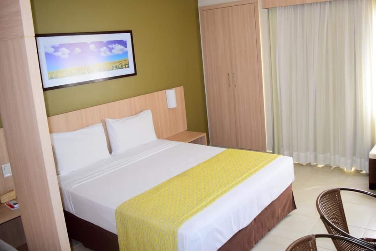 Quarto de hotel com cama, mesa de cabeceira, cadeira e guarda-roupa.