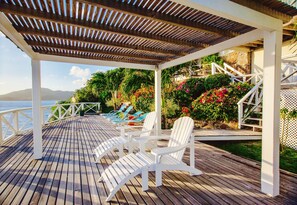 Um deck de madeira com cadeiras brancas e vista para o mar.
