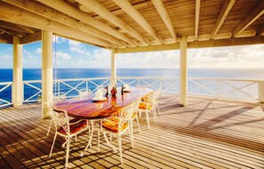 Um deck de madeira com mesa e cadeiras, com vista para o oceano.
