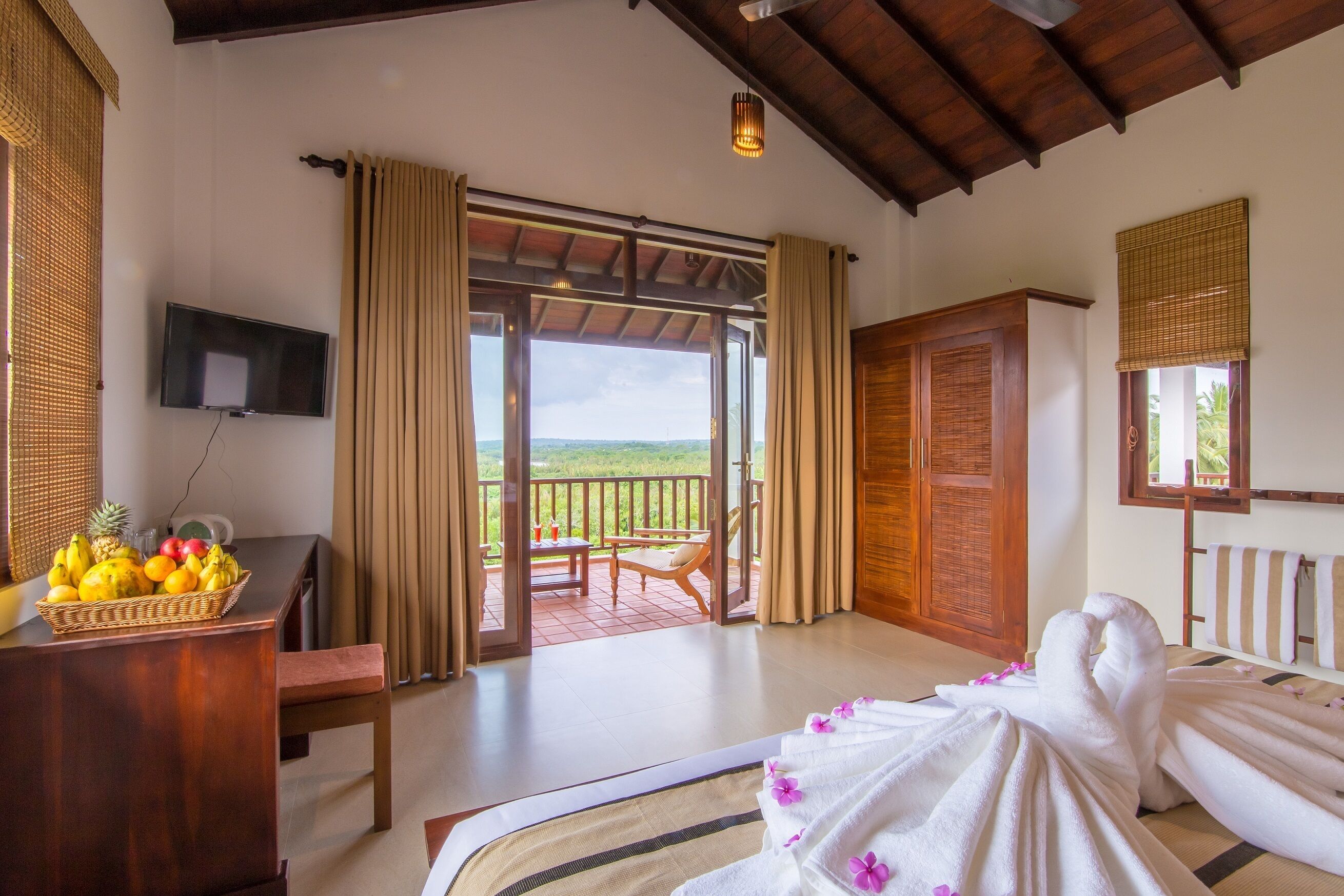 Quarto de hotel com cama, escrivaninha com frutas, televisão e varanda com vista.