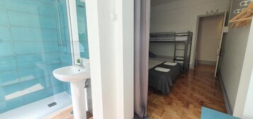 Casa de banho com lavatório, chuveiro e janela. Apresenta uma cama beliche com uma toalha.