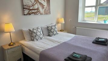 Quarto com uma cama, duas luminárias de cabeceira, uma janela e uma obra de arte na parede.