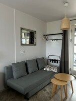 Quarto moderno e minimalista com um sofá cinza, uma pequena mesa de madeira, um candeeiro pendente e um espelho na parede.