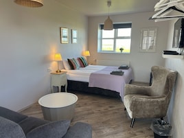 Quarto com cama, luminárias de cabeceira, uma cadeira, mesa redonda e janela com persianas.