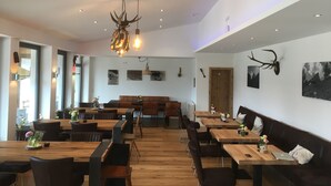Um restaurante espaçoso com mesas e bancos de madeira, um lustre de veado único e obras de arte fixadas na parede.