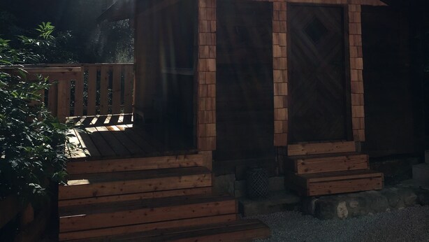 Uma cabana de madeira com telhado inclinado, deck de madeira e chão de cascalho.