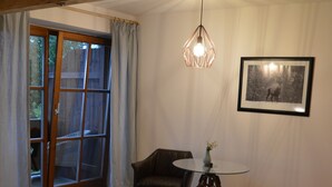 Quarto com teto de madeira, porta de vidro que dá para o exterior, sofá de couro preto, mesa de vidro com um vaso, quadro na parede e tapete de couro.