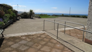 Uma área pavimentada com guarda-corpo de metal, um portão e vista para o mar.