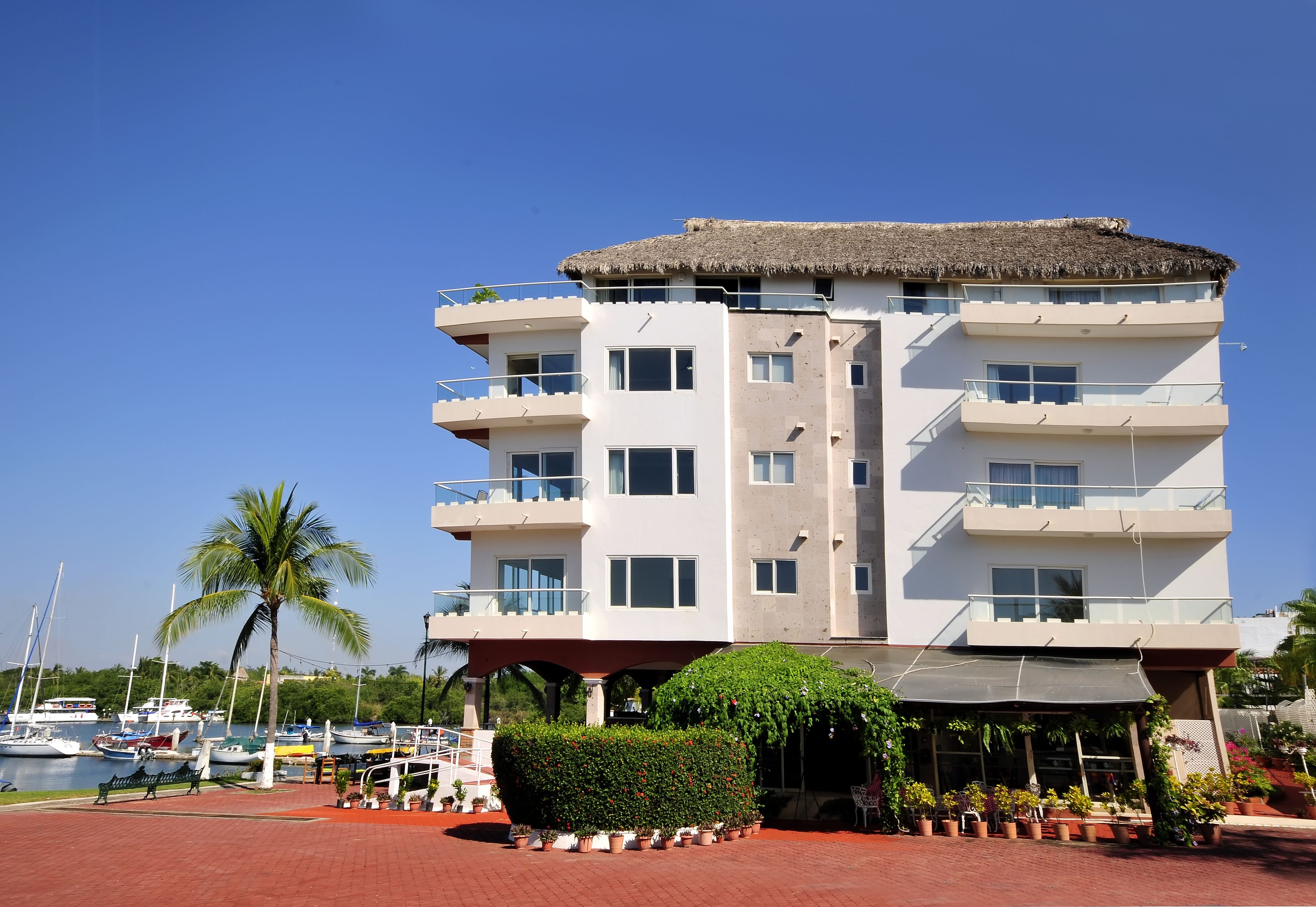 Um hotel com vários andares, telhado de palha, varandas e um cais com barcos.