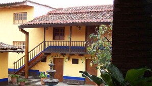 Um pátio com uma fonte, plantas em vasos, uma escadaria e um edifício com telhado e varandas.