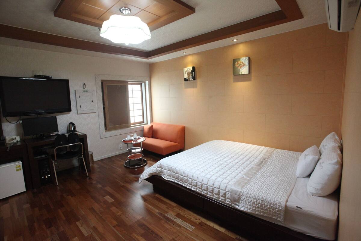 Quarto com cama, televisão, escrivaninha e cadeira.